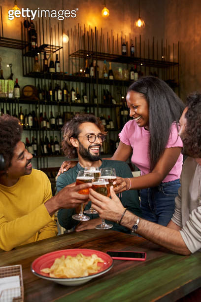 Vertical photo of group co-workers toast with beer at restaurant bar ...