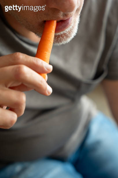 A man takes a bite from a carrot 이미지 (1727740649) - 게티이미지뱅크