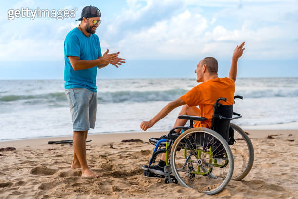 A disabled person in a wheelchair on the beach with a friend having fun ...