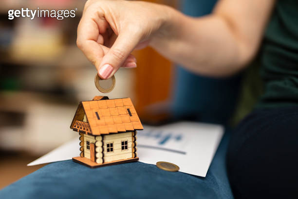 Hand putting coin in house model of coin for saving money for buying ...
