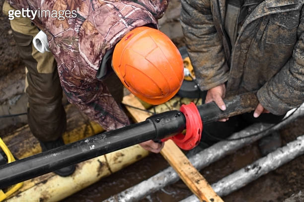 Worker in helmet repairs communal water pipe in trench on street. Work ...
