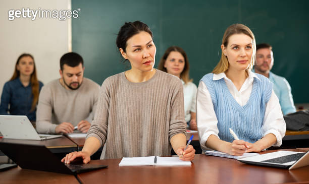 Students writing in notebook and typing on laptop during class in ...