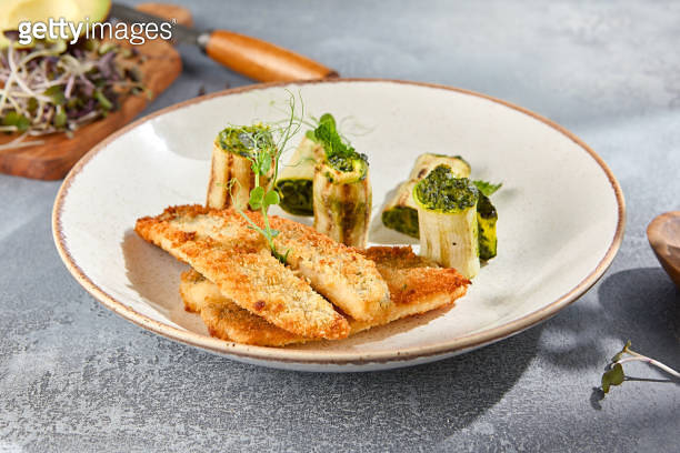 Closeup side view of grilled perch with zucchini rolls on a ceramic ...