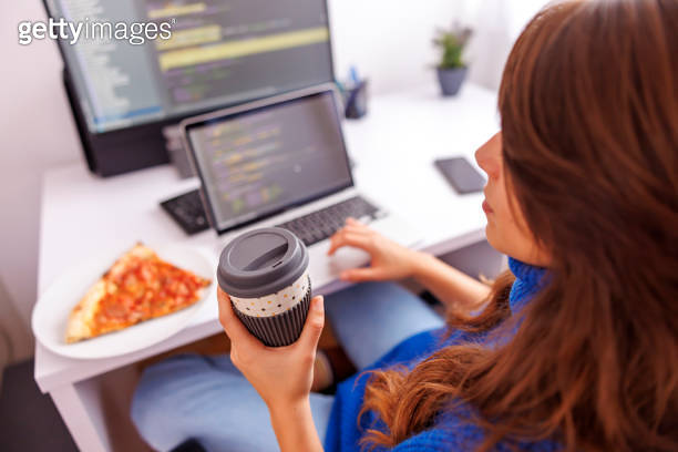 Female programmer drinking coffee and eating pizza while working ...