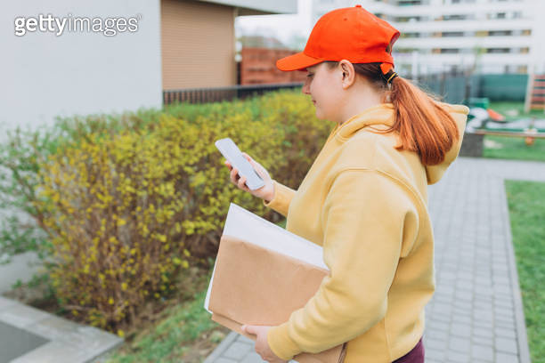Happy Delivery woman with smartphone and parcel in hands front of the ...