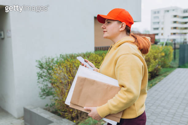 Happy Delivery woman with smartphone and parcel in hands front of the ...