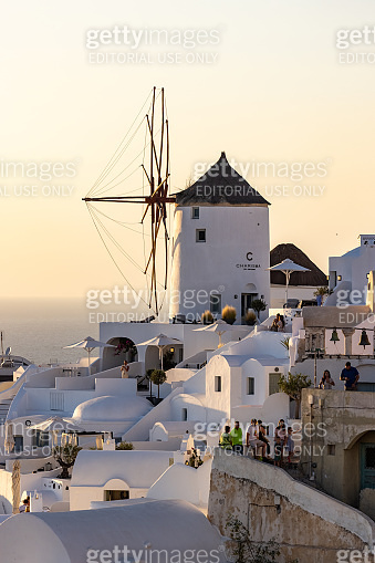 Whitewashed houses and windmills in Oia in warm rays of sunset on ...