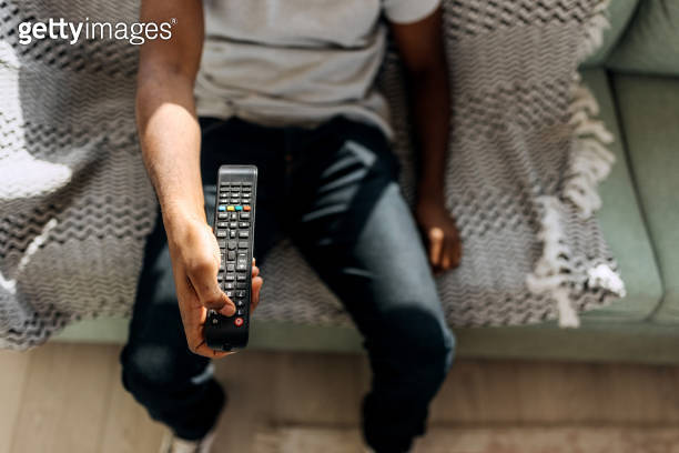 Man using TV remote while sitting on a sofa at home 이미지 (1571812304 ...