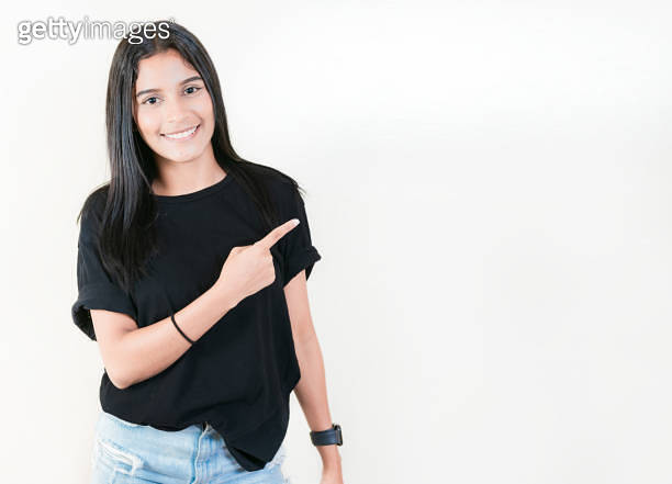 Smiling teenage girl pointing side with hand. Cheerful latin girl ...