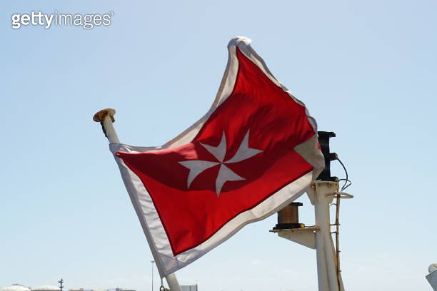 Merchant flag of Malta, red banner with white Maltese cross, flying in ...