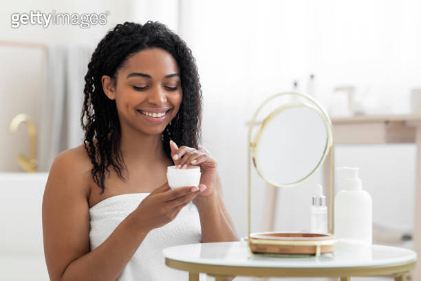 Black woman making beauty treatments at home, taking moisturising cream ...