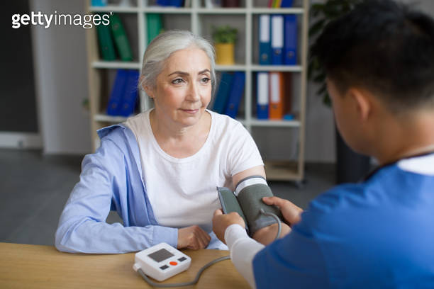 Adult asian therapist measures blood pressure of old european lady ...
