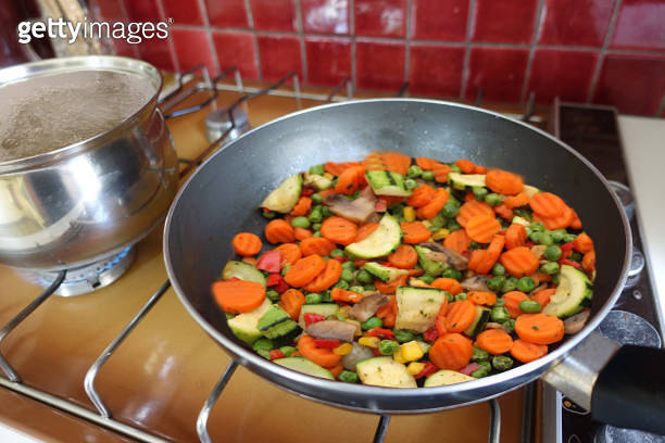 Portioned mixed vegetables being cooked and a pot of boiling water on a ...