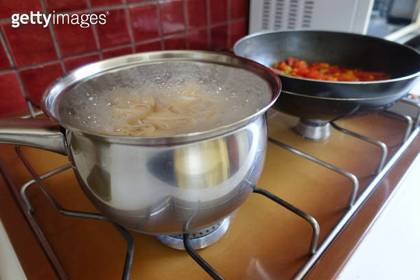 Tagliatelle pasta being cooked in boiling water and homemade tomato ...