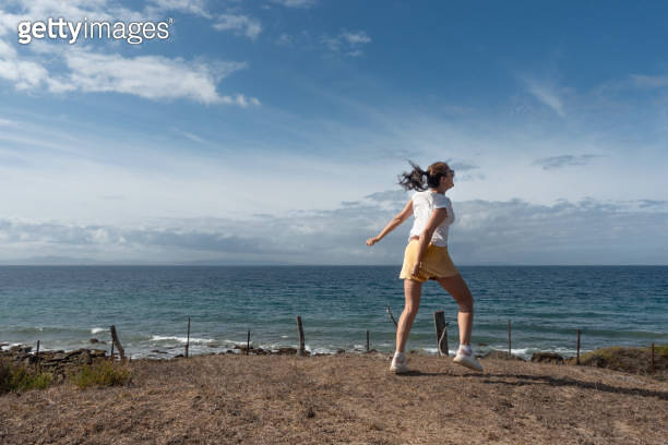 A confident woman jumps on the shore of the ocean, expressing self ...