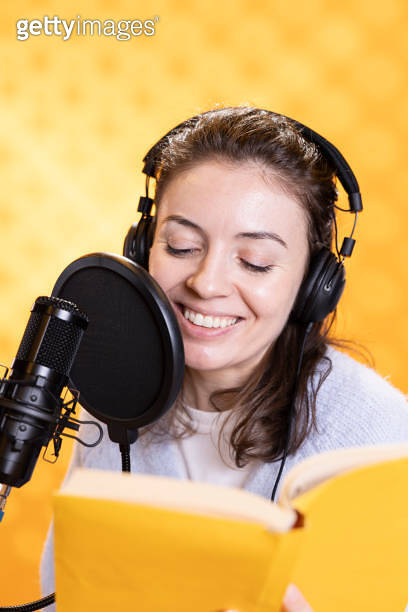 Happy narrator wearing headphones reading aloud from book into mic ...