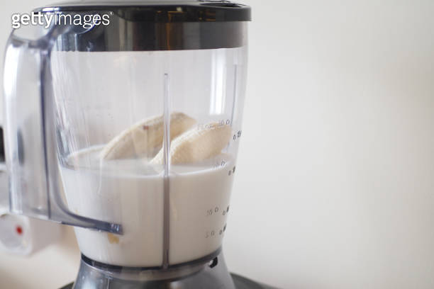 Person making smoothie in blender with food and liquid in kitchen ...