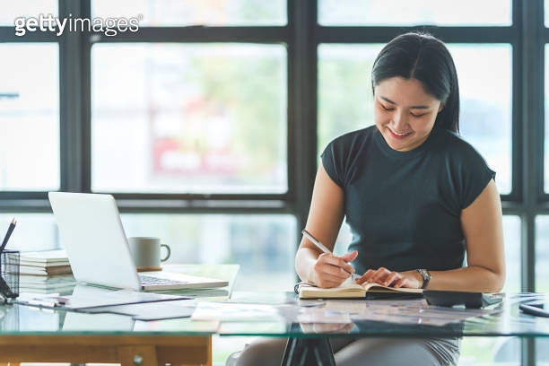 A young female administrative assistant making notes of working ...