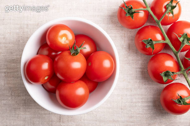 Red cherry tomatoes, small cocktail tomatoes in a white bowl on linen ...