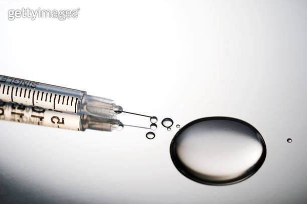 Injection syringe with a drop of drug on a stainless steel background ...