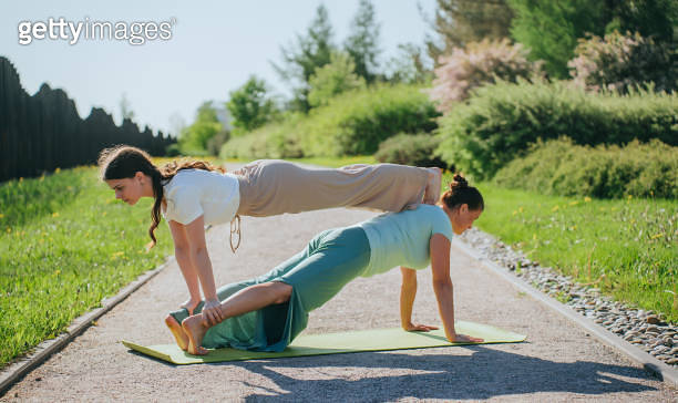 Two women practicing partner yoga outdoors, building balance and ...