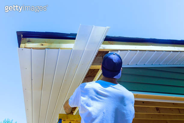 Mounting vinyl soffit plastic boards to roof rafters on a ceiling house ...