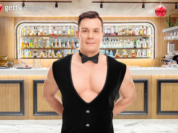 Male butler with a black vest and bow-tie standing in front of a bar ...