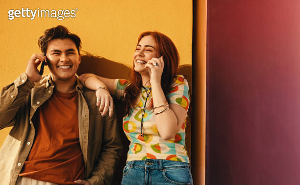 Two friends happily using smartphones and talking on the phone outdoors ...