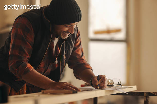 Mature contractor drawing on blueprints with a pencil, creating a home ...