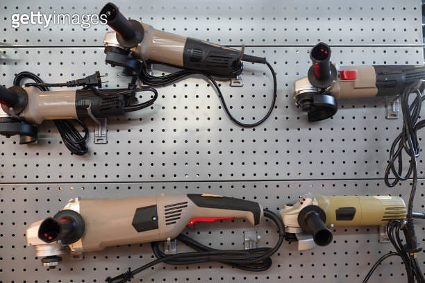 A collection of electric grinders hanging on a perforated wall display ...