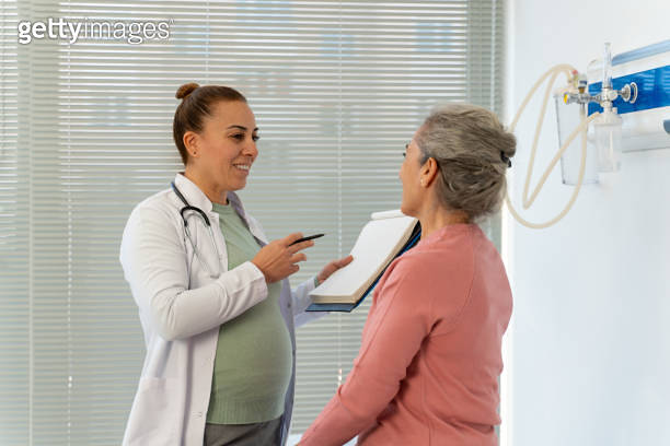 Pregnant female doctor informing her elderly female patient about test ...