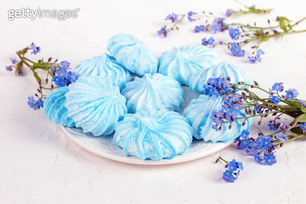 A plate of blue meringues sits on a white table next to a bouquet of ...