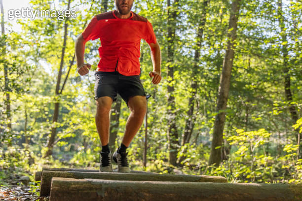 Man jumping over logs on a wooden exercise station along an outdoor ...