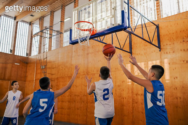 Junior basketball players shooting a ball at the hoop during their ...