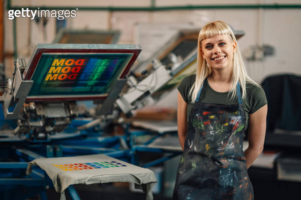 Portrait of happy print shop worker standing near screen printing press ...