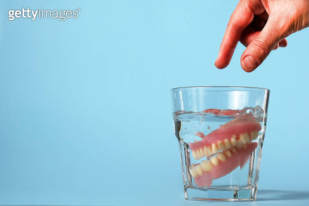 Close-up of a hand putting artificial teeth in water glass 이미지 ...