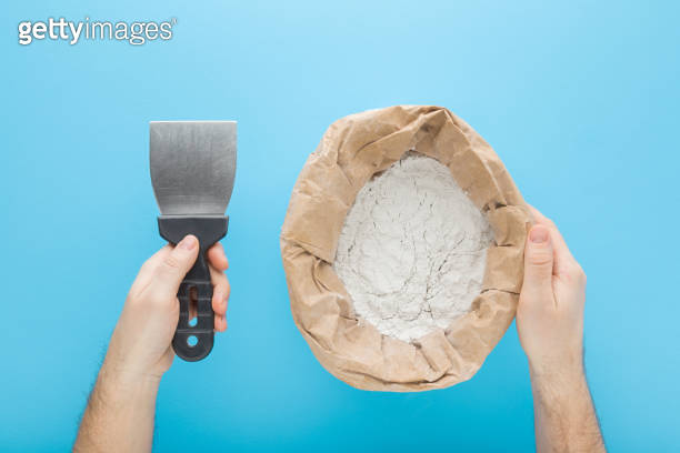Man hands holding spatula and opened paper bag of white dry finishing ...