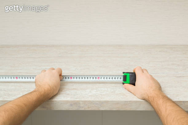 Young man hands holding measure tape and measuring surface of beige ...