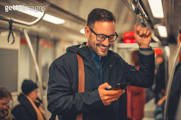 A cheerful adult businessman typing text messages on his phone while ...