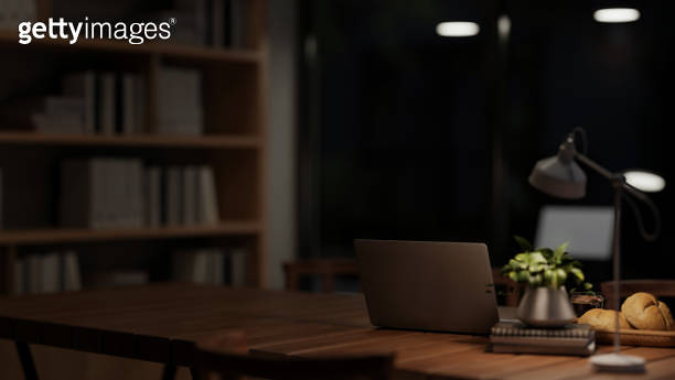 A laptop computer on a meeting table under a dim light from a table ...