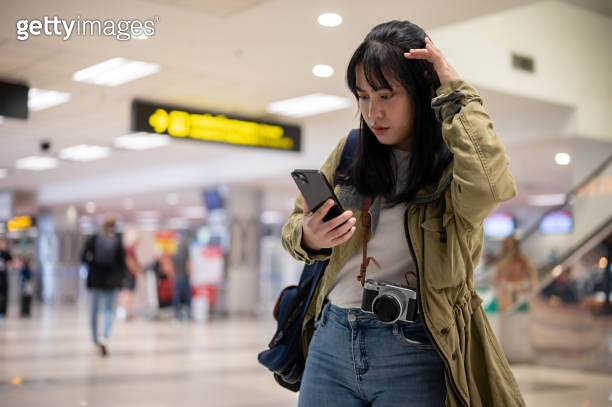 A confused female is reading her flight information on her phone with a ...