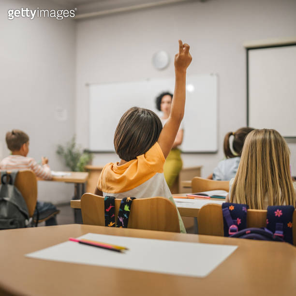 Young boy student raise his hand to answer a question during a lesson ...