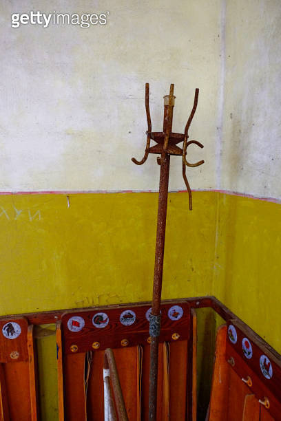 The image shows a rusted metal coat rack in a room with a yellow wall ...