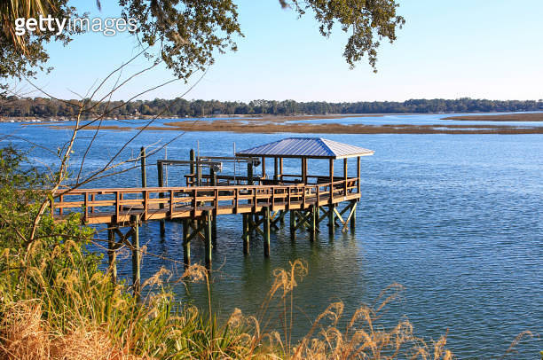 A wooden pier in Bluffton South Carolina extends over a calm body of ...