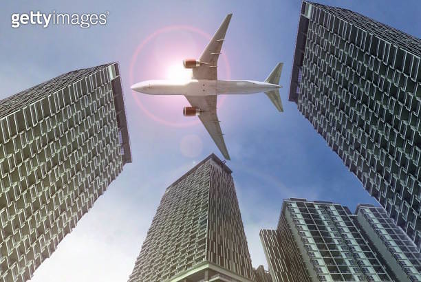 Airplane flying over high-rise buildings with bright sunlight in ...