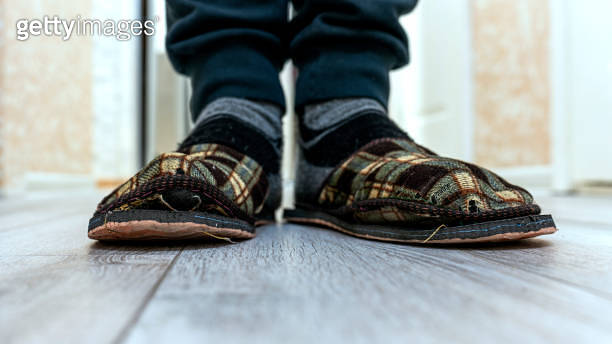 Person wearing worn out slippers and socks standing on wooden floor ...