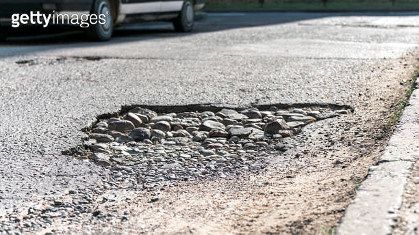 Large pothole on asphalt road with exposed rocks and uneven surface ...