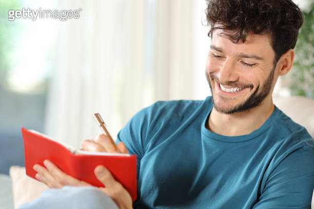 Happy man writing in agenda sitting at home 이미지 (2151674643) - 게티이미지뱅크