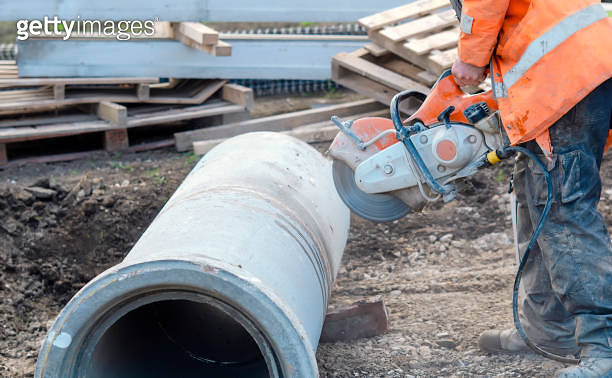 Construction worker cutting concrete pipe for drainage using a cut-off ...