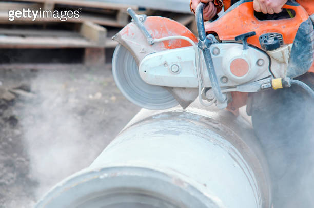 Construction worker cutting concrete pipe for drainage using a cut-off ...